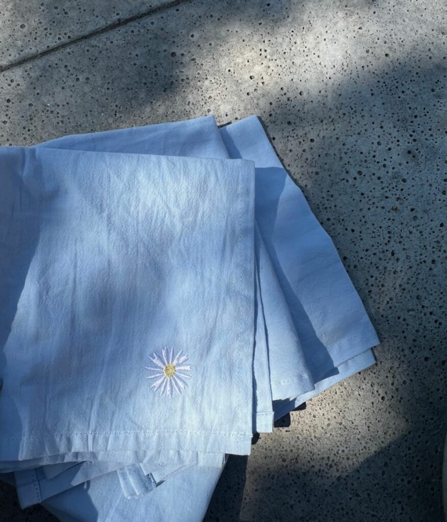 Hellblaue Serviette mit Gänseblümchen-Stickerei.