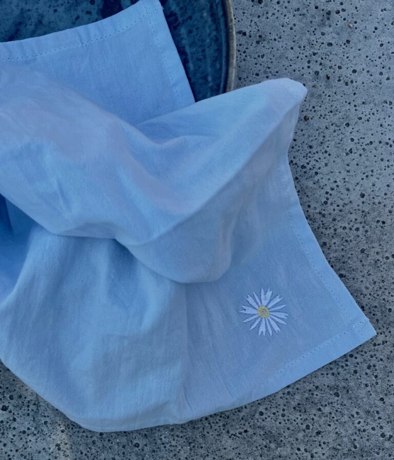 Hellblaue Serviette mit Gänseblümchen-Stickerei.